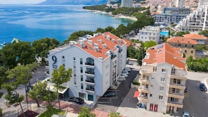 Um edifício de vários andares com varandas, estacionamento e vista para o mar e montanhas.