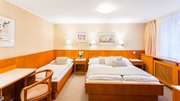 Quarto de hotel com uma cama grande, uma escrivaninha, uma cadeira, duas mesas de cabeceira e duas luminárias fixadas na parede.