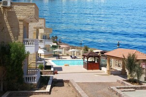 Área da piscina com vista para o mar, um gazebo e um edifício com fachada de pedra.