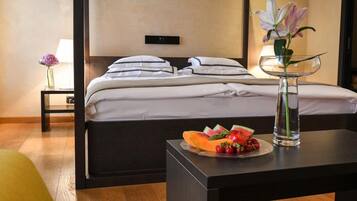 Quarto de hotel com cama bem arrumada, mesa de cabeceira com um prato de frutas e um vaso com flores.