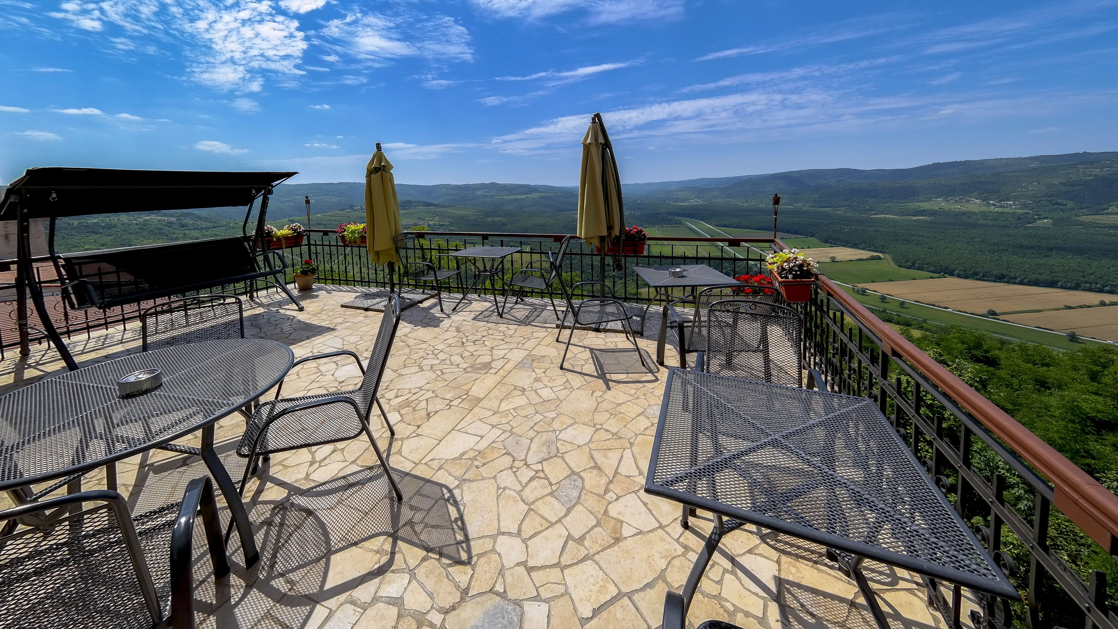 Um terraço com área de estar ao ar livre, piso de pedra e uma vista panorâmica de colinas e campos.
