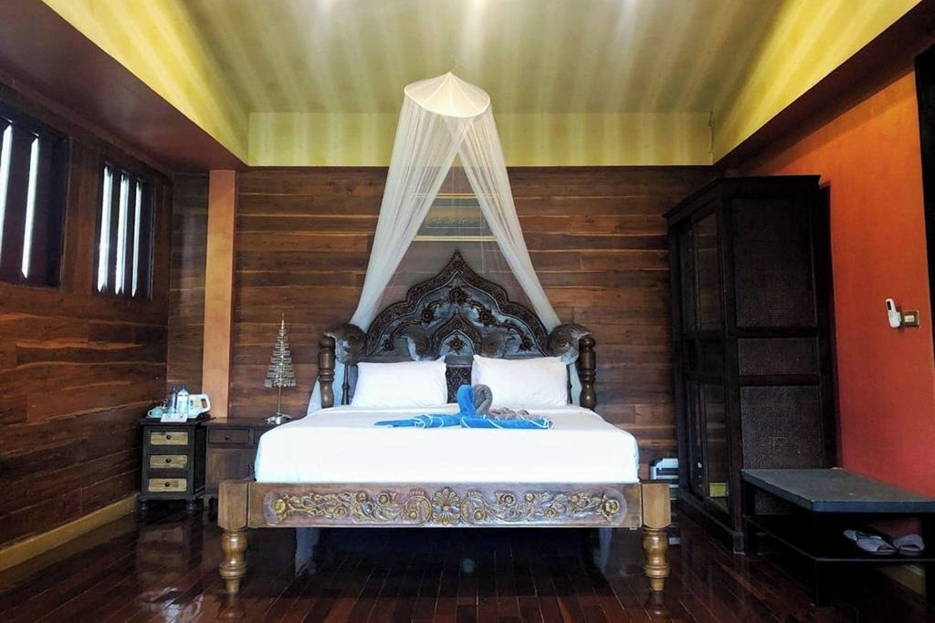 Quarto com painéis de madeira, uma cama grande, um dossel e uma mesa de cabeceira com abajur.