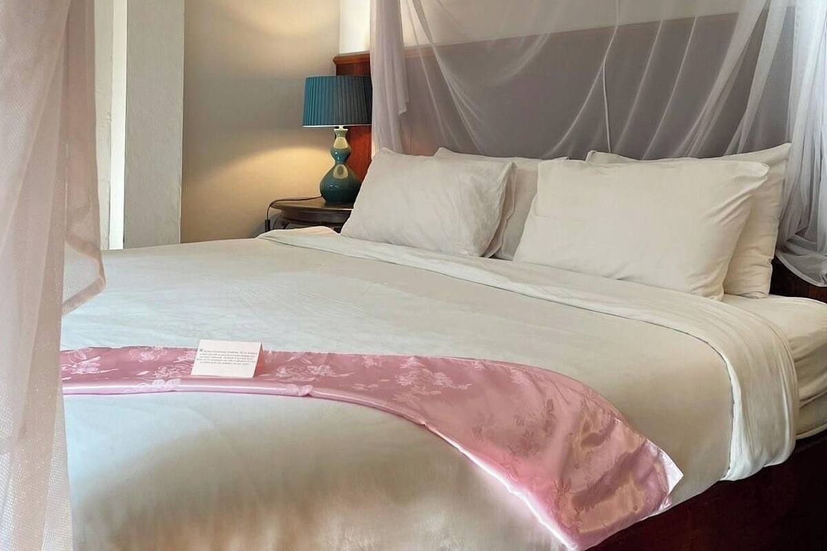Cama bem arrumada com lençóis brancos e almofada decorativa rosa.