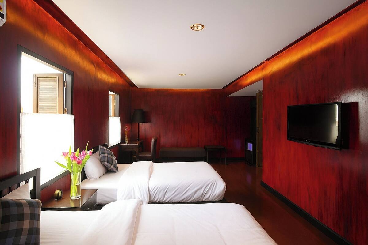 Quarto de hotel com duas camas, televisão, escrivaninha e janela com vista.