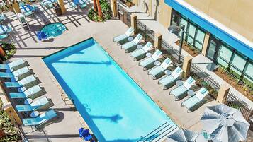 Área de piscina no terraço com espreguiçadeiras e guarda-sóis, cercada por uma grade e um edifício com janelas amplas.