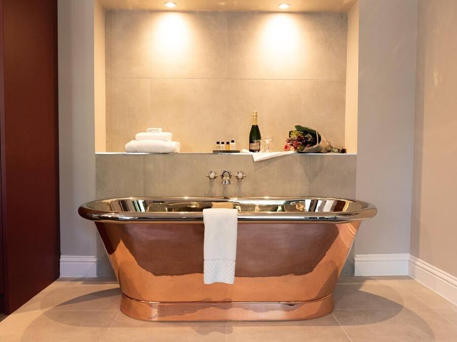 Um banheiro moderno com uma banheira de cobre independente, um porta-toalhas e uma prateleira com produtos de higiene pessoal.