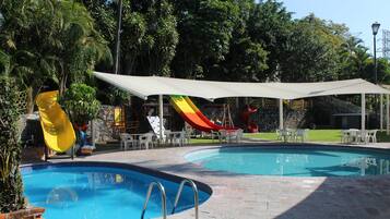 Área de piscina com duas escorregas e zona de estar coberta.