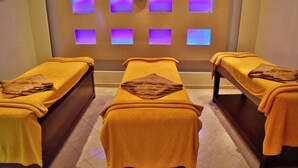 Um quarto com três macas de massagem, cada uma com uma toalha amarela e um travesseiro marrom.