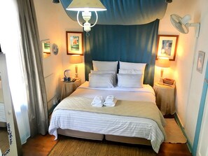 Cama bem arrumada com colcha, duas mesas de cabeceira com luminárias e um ventilador de teto.
