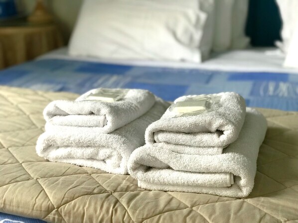 Uma cama bem arrumada com um edredom bege e duas toalhas brancas dobradas por cima.