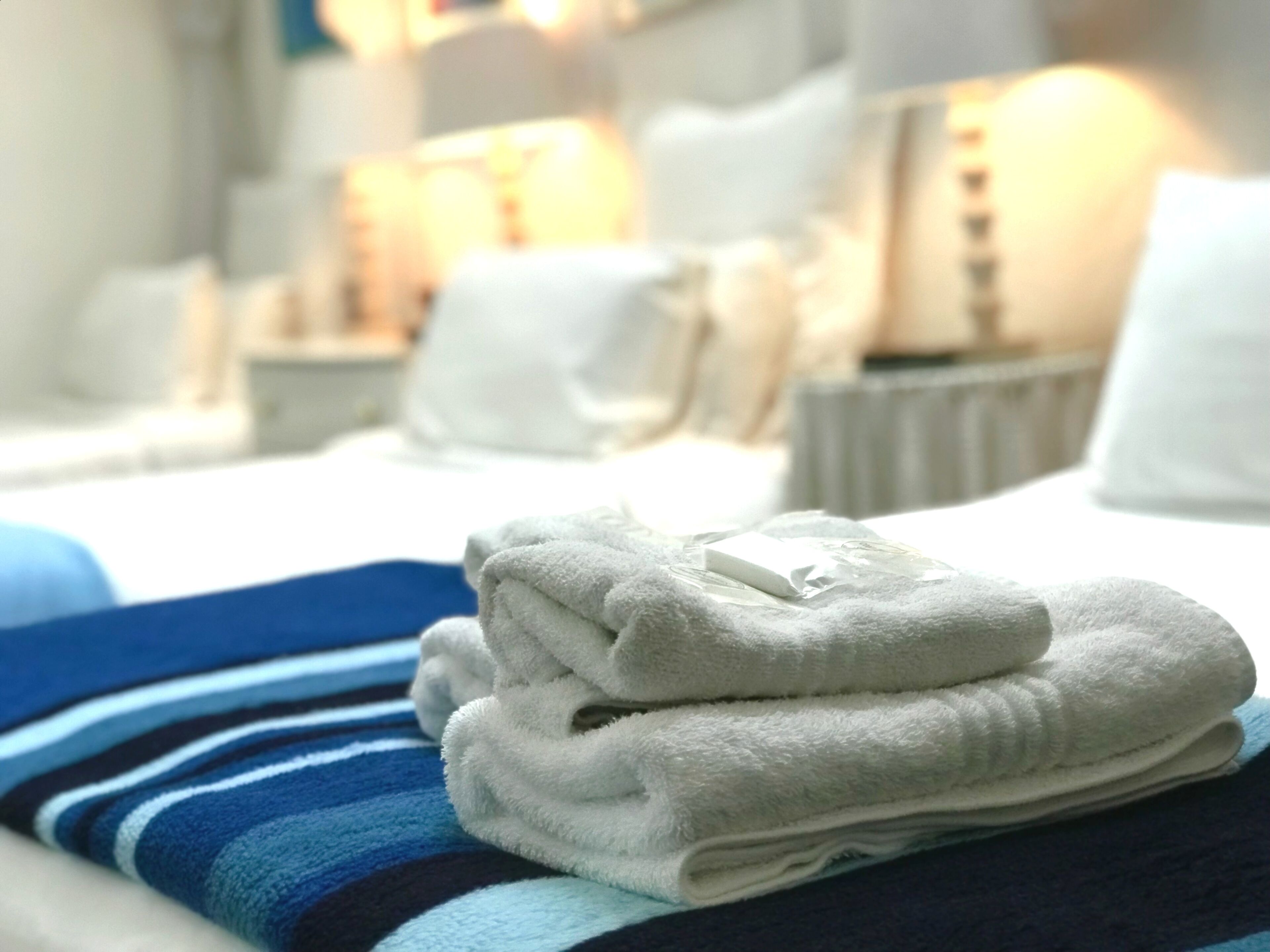Cama bem arrumada com toalhas brancas e manta azul listrada.