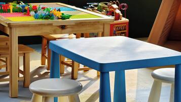 Um quarto com uma janela grande, uma mesa de madeira com brinquedos coloridos e uma mesa azul.