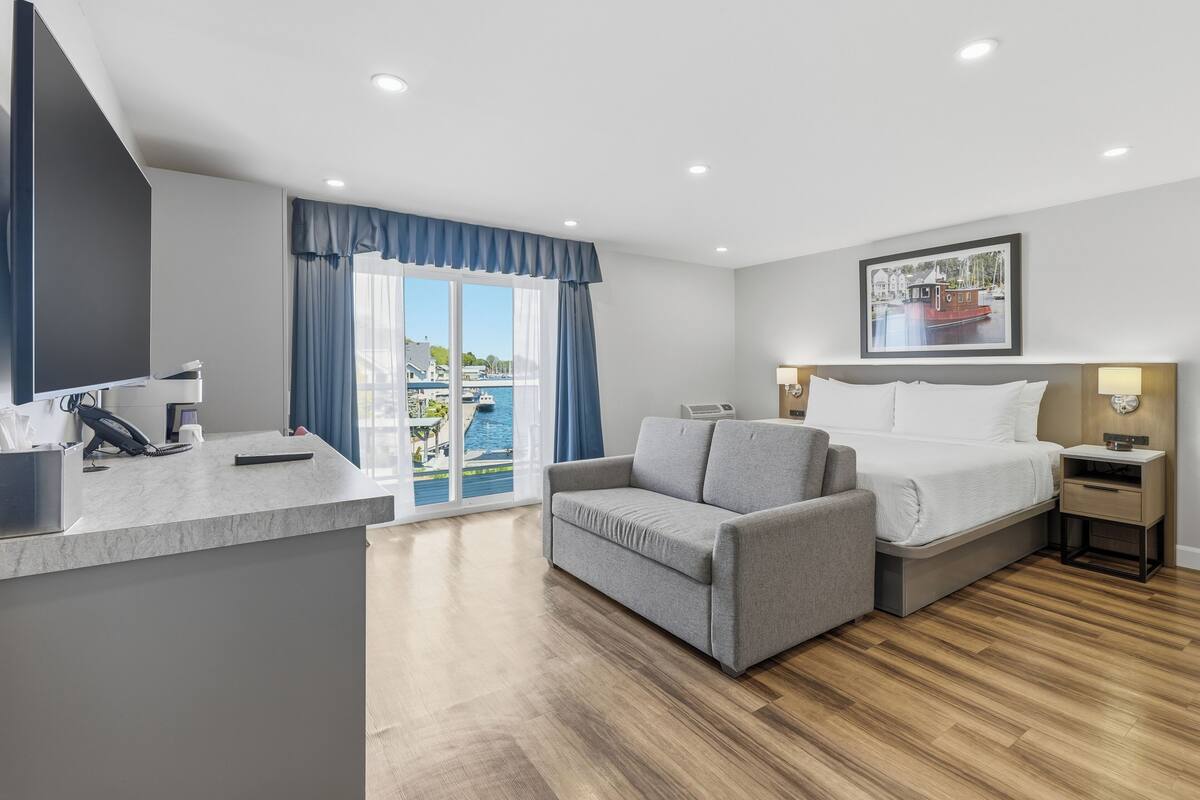 Quarto de hotel com uma cama, um sofá, uma mesa com telefone e uma janela com vista para o mar.