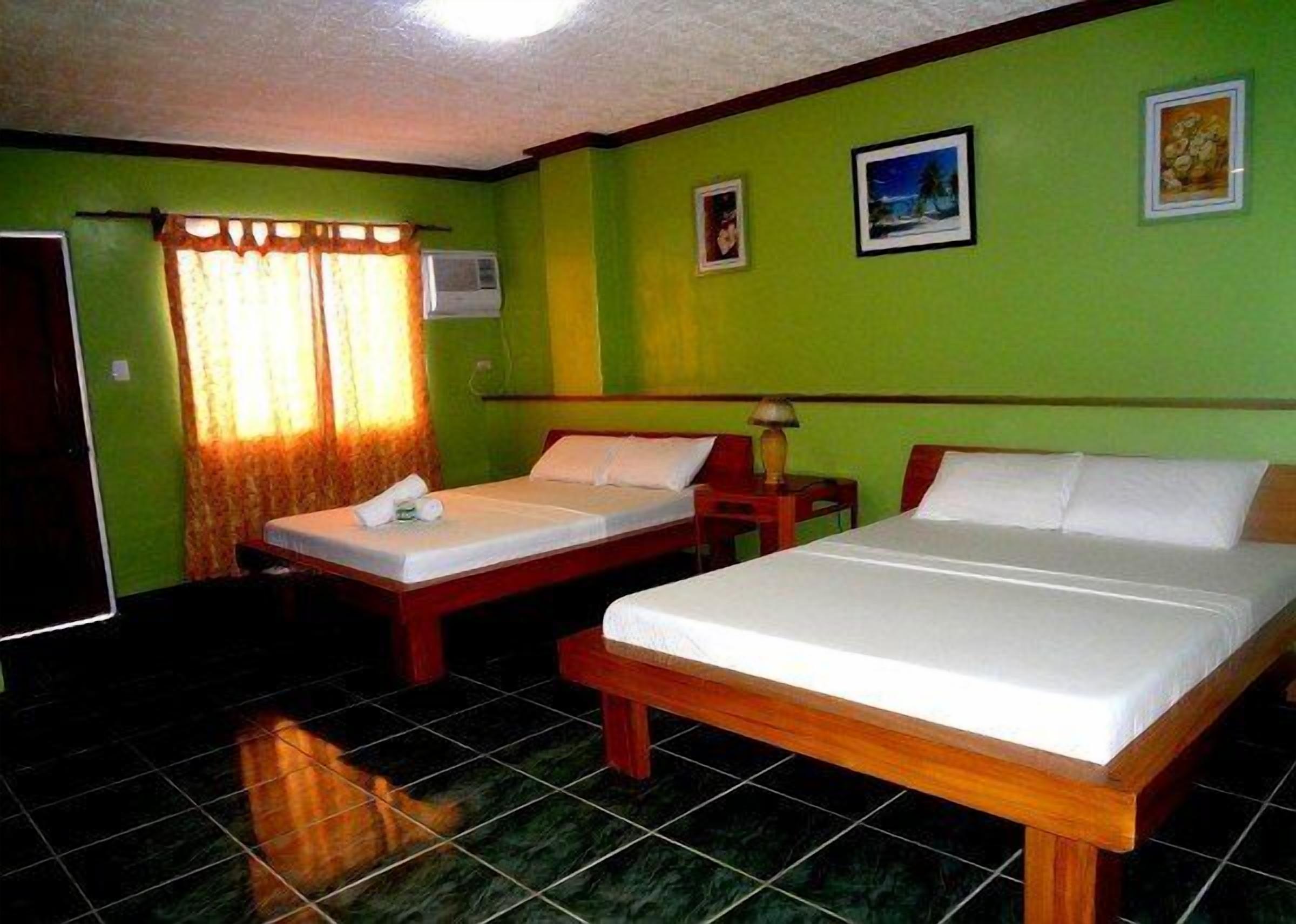 Quarto com duas camas, uma janela com cortinas, ar-condicionado fixado na parede e uma mesinha com abajur.