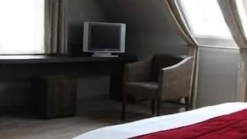 Quarto de hotel com cama, escrivaninha com televisão e uma cadeira.