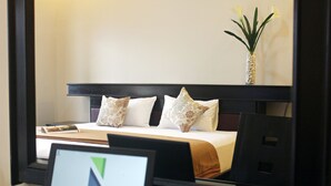 Quarto de hotel com uma cama, almofadas, um vaso com flores e uma placa com o nome do hotel.