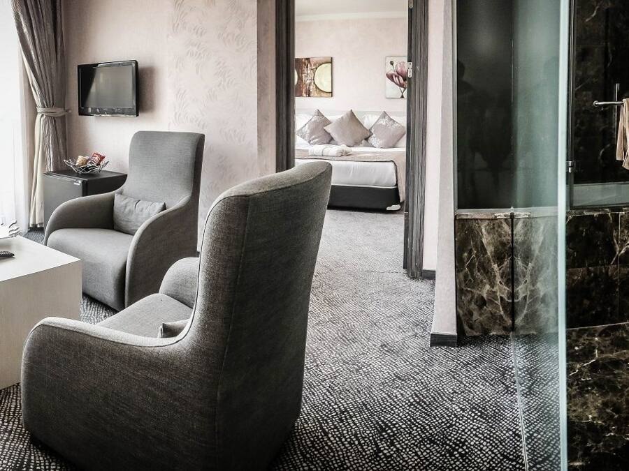 Quarto de hotel com área de estar, televisão, cama e banheiro com chuveiro e pia.