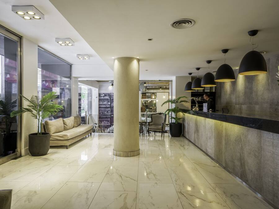 Um hall moderno com piso de mármore, um pilar grande, um balcão de recepção e uma área de estar com sofá e cadeiras.