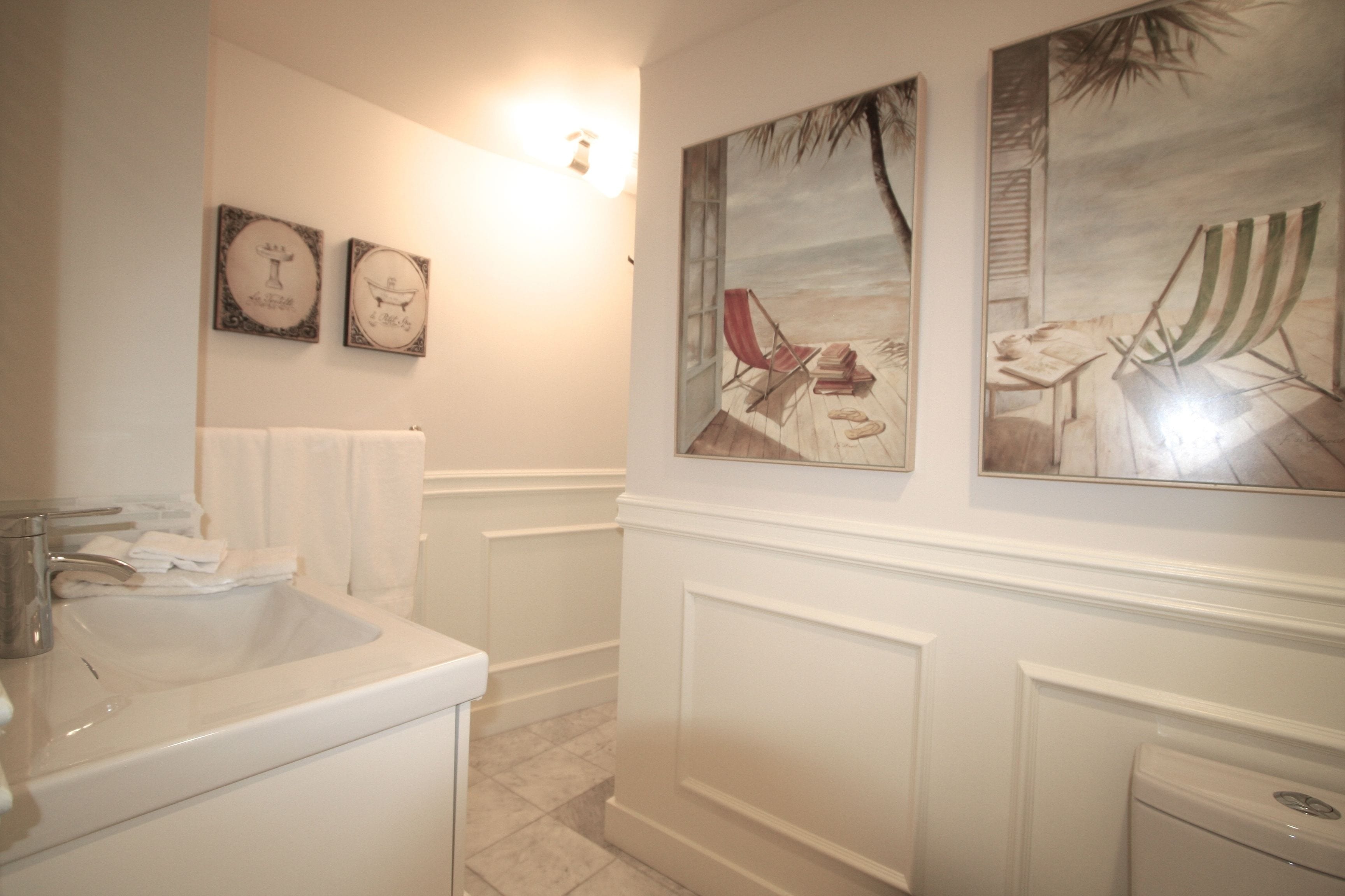 Casa de banho com lavatório, porta-toalhas e duas imagens emolduradas na parede.