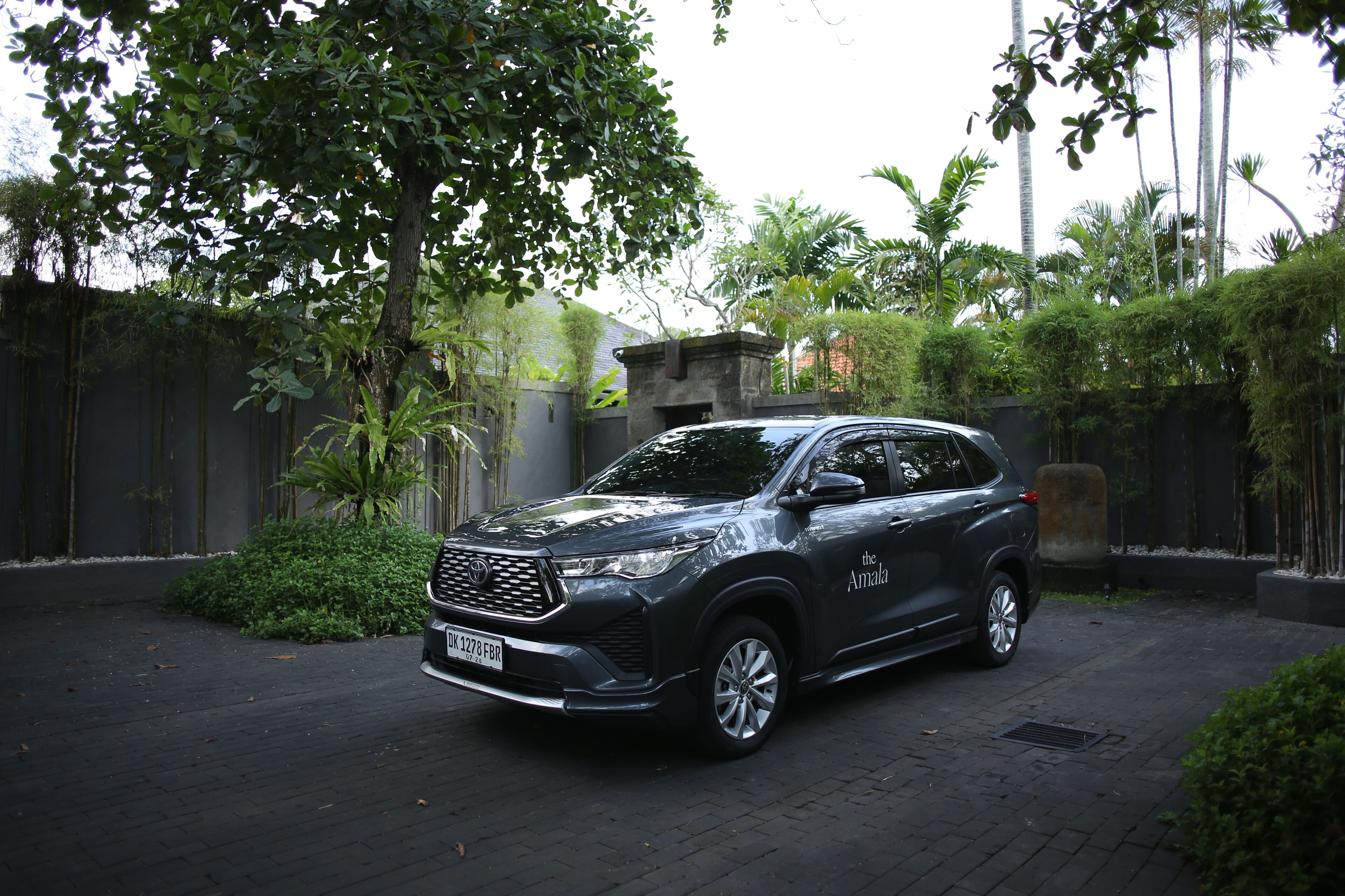 Um SUV preto estacionado em uma entrada com um muro de pedra e vegetação ao fundo.
