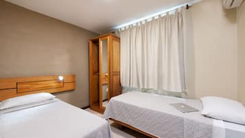 Quarto de hotel com duas camas de solteiro, cabeceira de madeira, espelho, guarda-roupa e janela com cortinas.