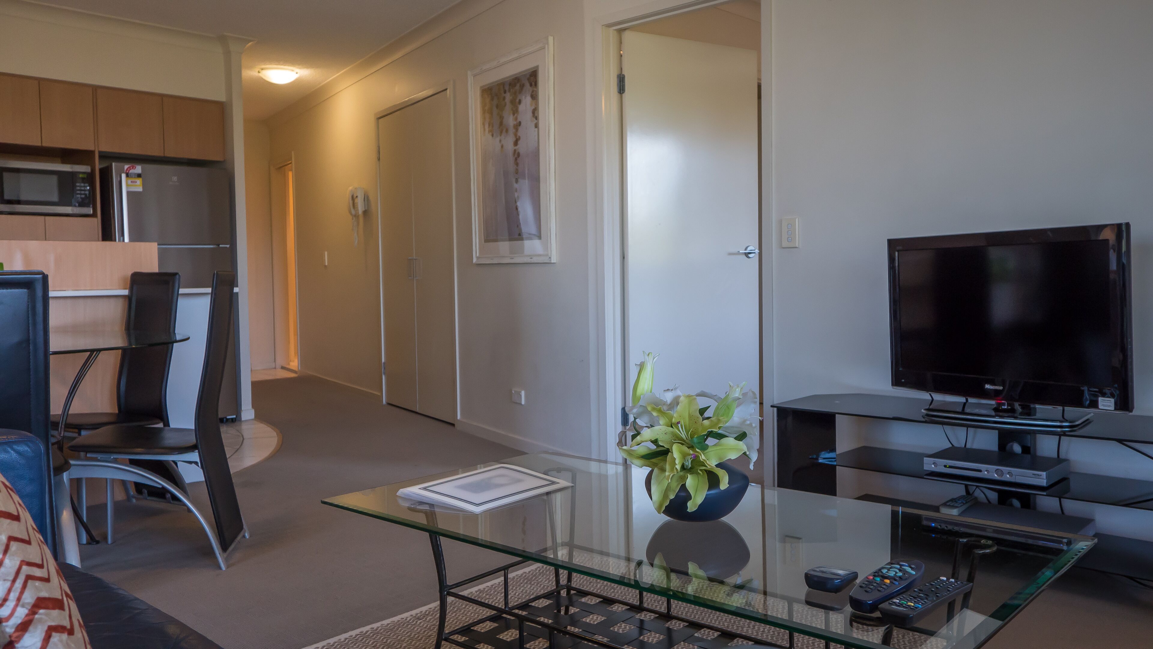Uma sala de estar moderna com uma mesa de centro de vidro, uma TV de tela plana e uma área de refeições com cadeiras e uma mesa.