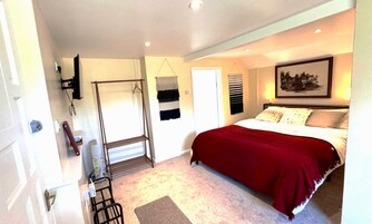 Quarto com uma cama, uma porta, um cabideiro e uma obra de arte pendurada na parede.