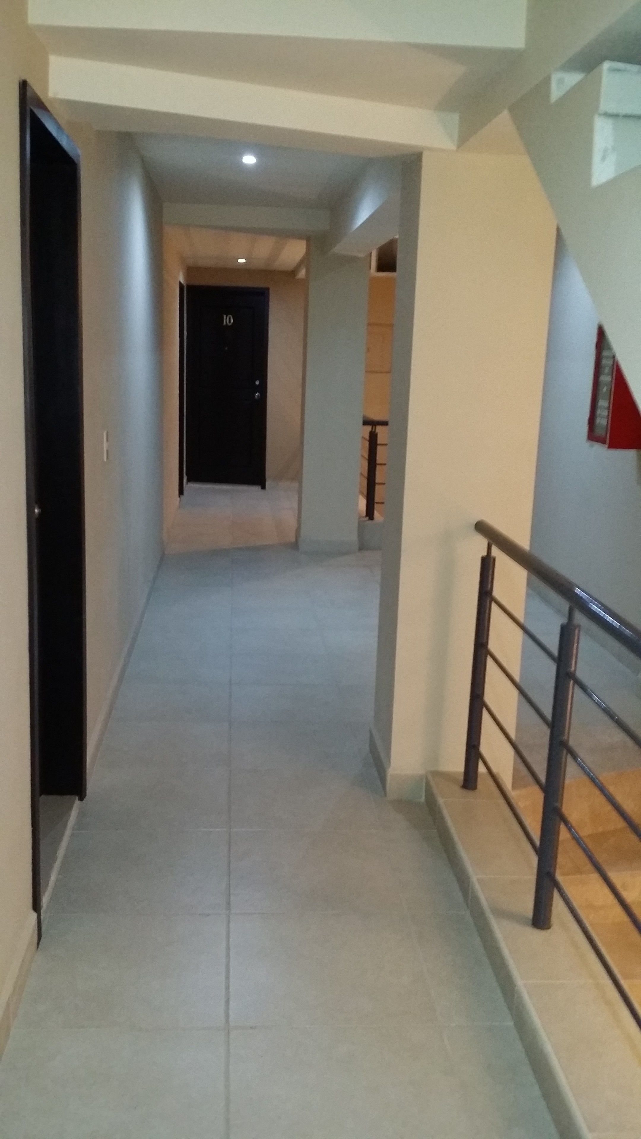 Um corredor com uma porta preta identificada com o número 10, uma escada com corrimão de metal e piso ladrilhado.