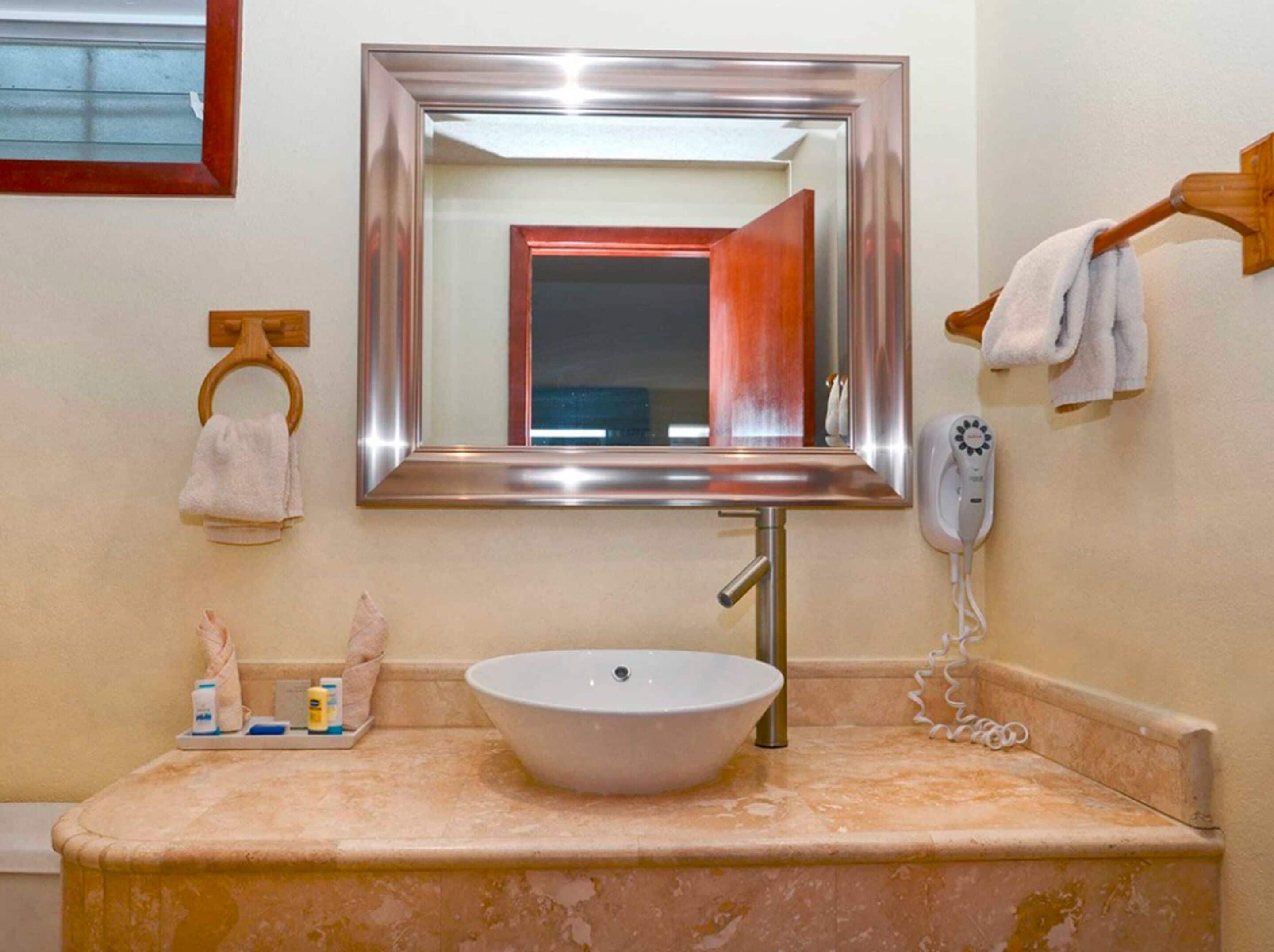 Casa de banho com um espelho grande, uma pia, um porta-toalhas, um secador de cabelo e produtos de higiene pessoal.