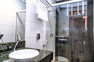 Casa de banho moderna com cabine de duche em vidro, lavatório com bancada de mármore e secador de mãos.
