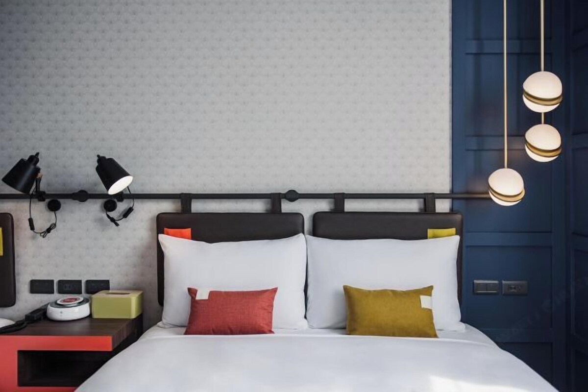 Quarto de hotel moderno com cama, mesas de cabeceira e uma luminária fixada na parede.