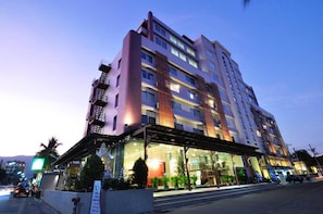 Um hotel de vários andares com design moderno, apresentando uma entrada coberta e uma escadaria visível que leva aos pisos superiores.