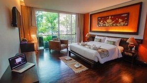 Quarto de hotel com uma cama, uma mesa com um laptop, uma janela grande e um quadro na parede.