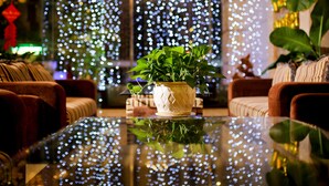 Um espaço de estar acolhedor, com uma mesa de vidro que reflete luzes, rodeado por sofás e uma planta em vaso.