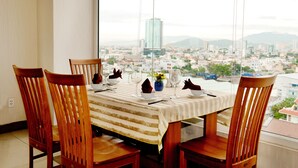Mesa de jantar posta para seis lugares, com cadeiras de madeira, toalha de mesa listrada e um vaso com flores.