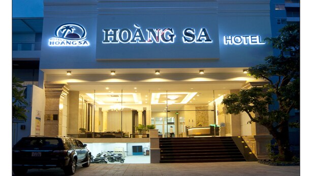 Um hotel com vários andares, janelas iluminadas e uma placa grande com a inscrição "Hoang Sa Hotel".