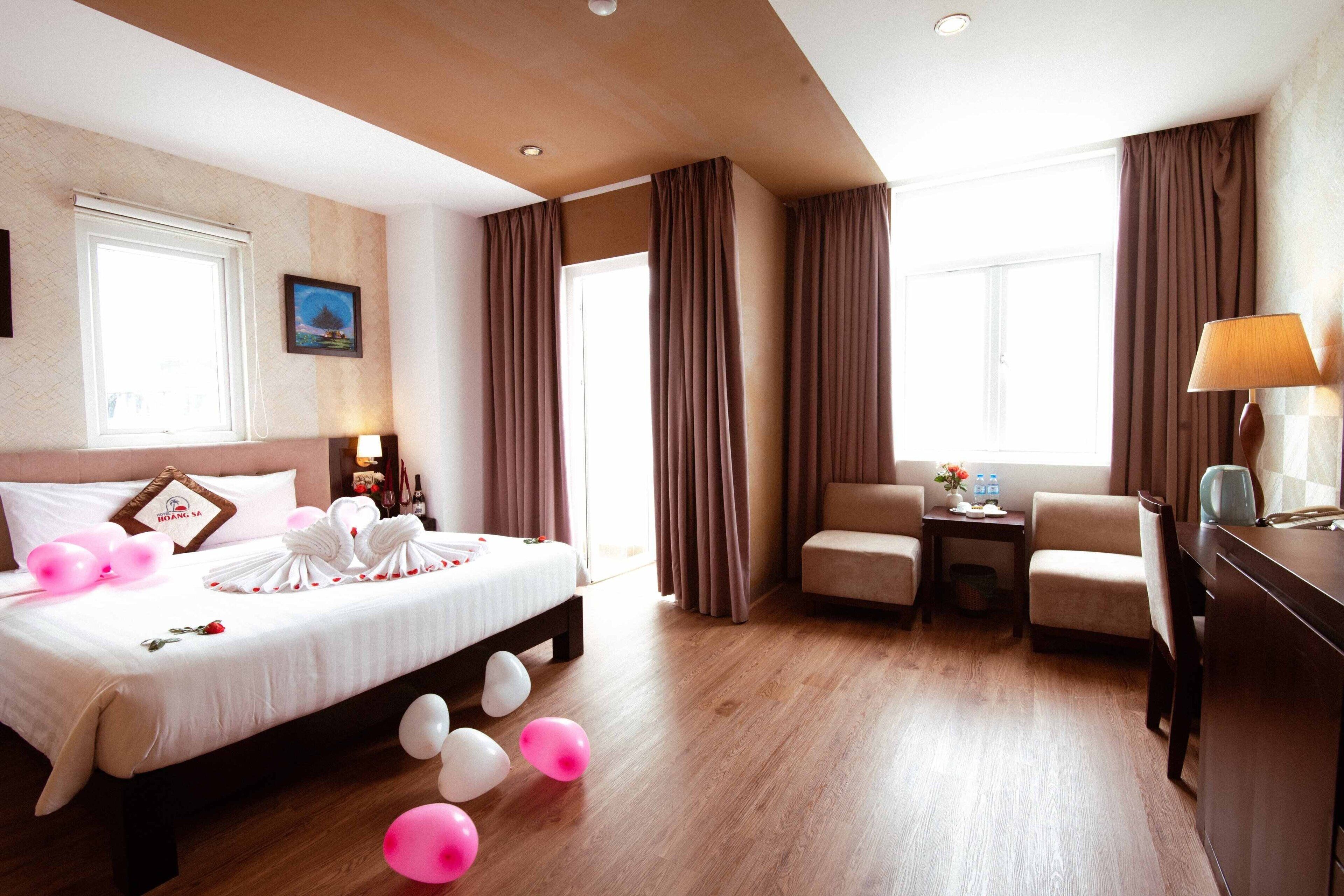 Quarto de hotel com uma cama grande, área de estar com sofá e poltronas, uma mesa pequena e uma escrivaninha com luminária.