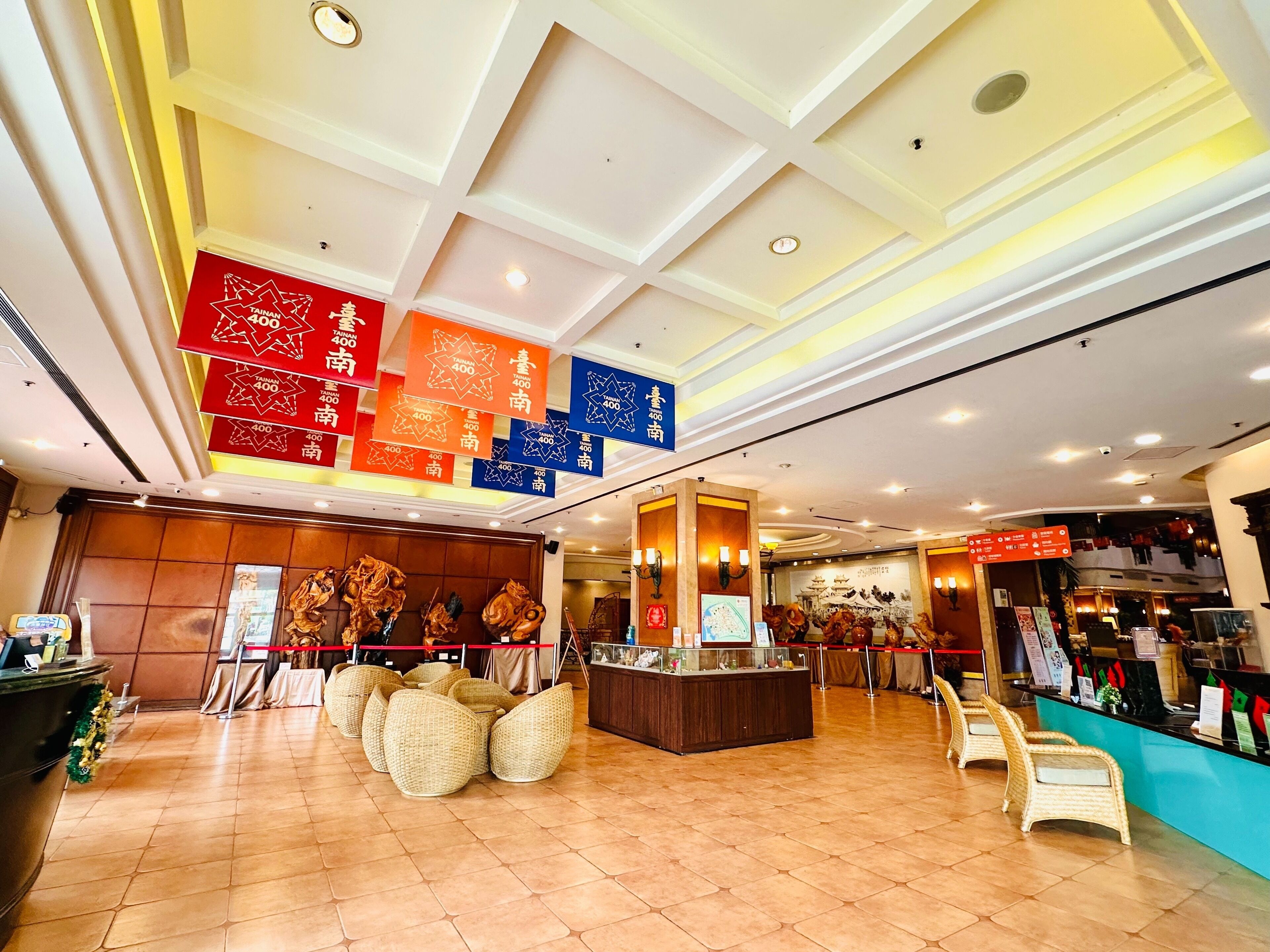 Um hall de hotel com balcão de recepção, cadeiras de vime e teto com banners pendurados.
