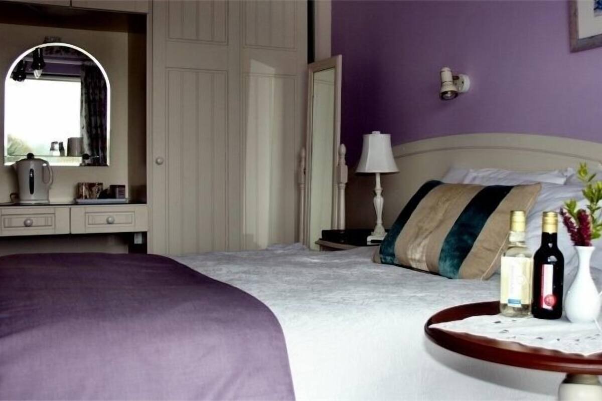 Um quarto com uma cama, uma mesa de cabeceira com uma garrafa e copos, uma luminária e um penteado.