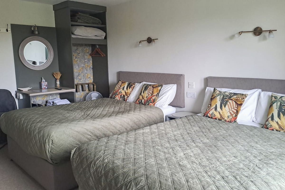 Quarto de hotel com duas camas, uma escrivaninha, um espelho e uma luminária na parede.