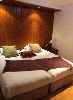 Uma cama com lençóis brancos, duas almofadas, um cobertor marrom e cabeceira de madeira.