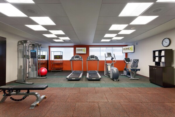 Uma academia com esteiras, aparelhos elípticos, um banco de musculação e uma bola de exercícios vermelha.