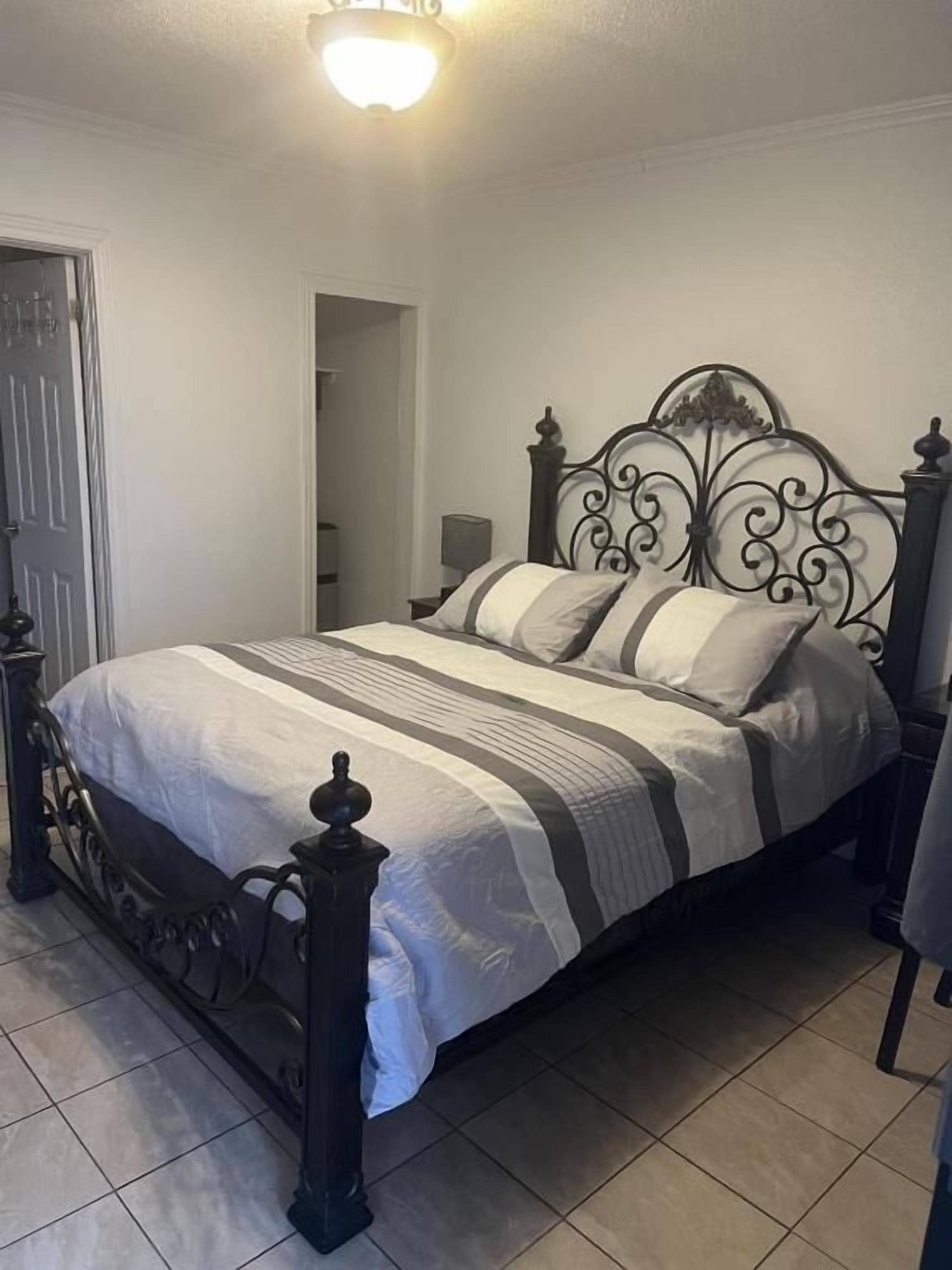 Quarto com cama, mesa de cabeceira, abajur e porta.