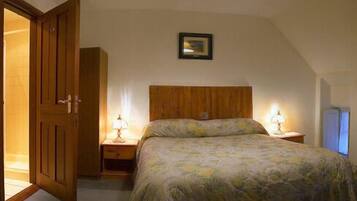 Quarto com cabeceira de madeira, cama com colcha floral, duas luminárias de cabeceira e um quadro pendurado na parede.