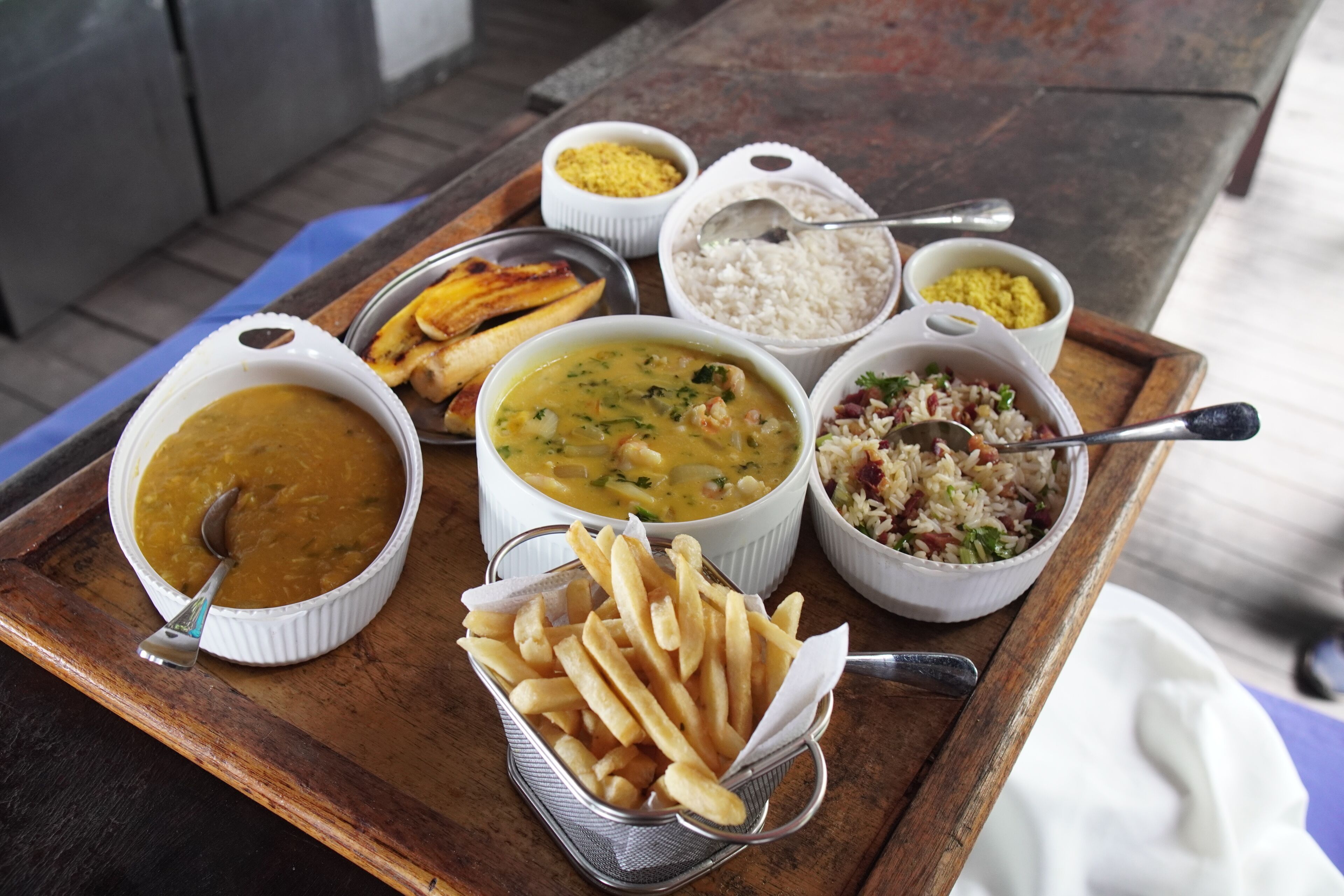 Uma bandeja de madeira com diversos pratos, incluindo arroz, sopa e batatas fritas.