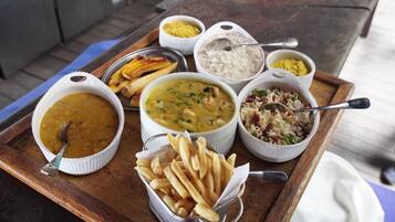 Uma bandeja de madeira com diversos pratos, incluindo arroz, sopa e batatas fritas.