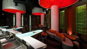 Uma área de bar moderna com mesas redondas, assentos e um teto iluminado em vermelho e verde.