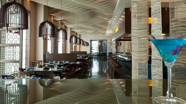 Interior moderno de restaurante com design de teto ondulado, luminárias pendentes e área de bar.