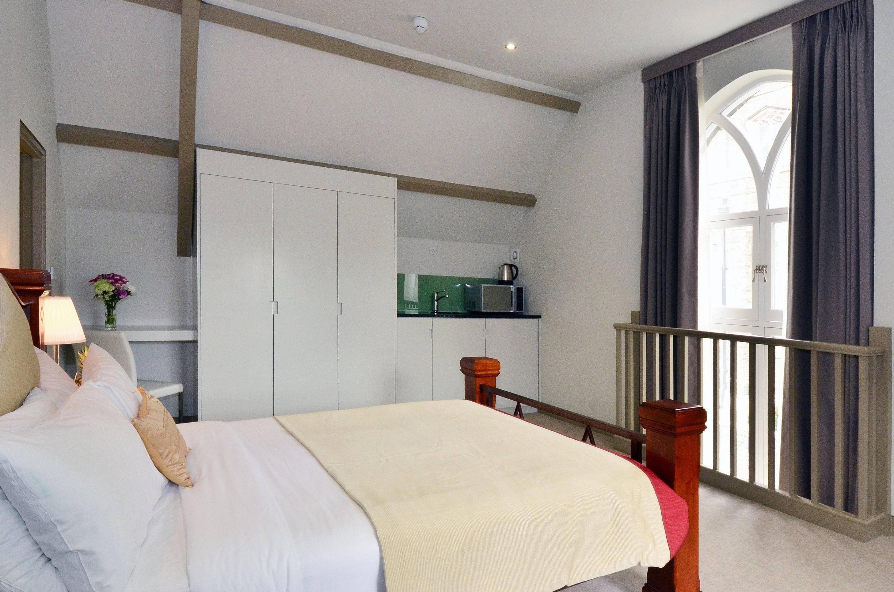 Quarto com cama, mesa de cabeceira, escrivaninha e janela com cortinas.