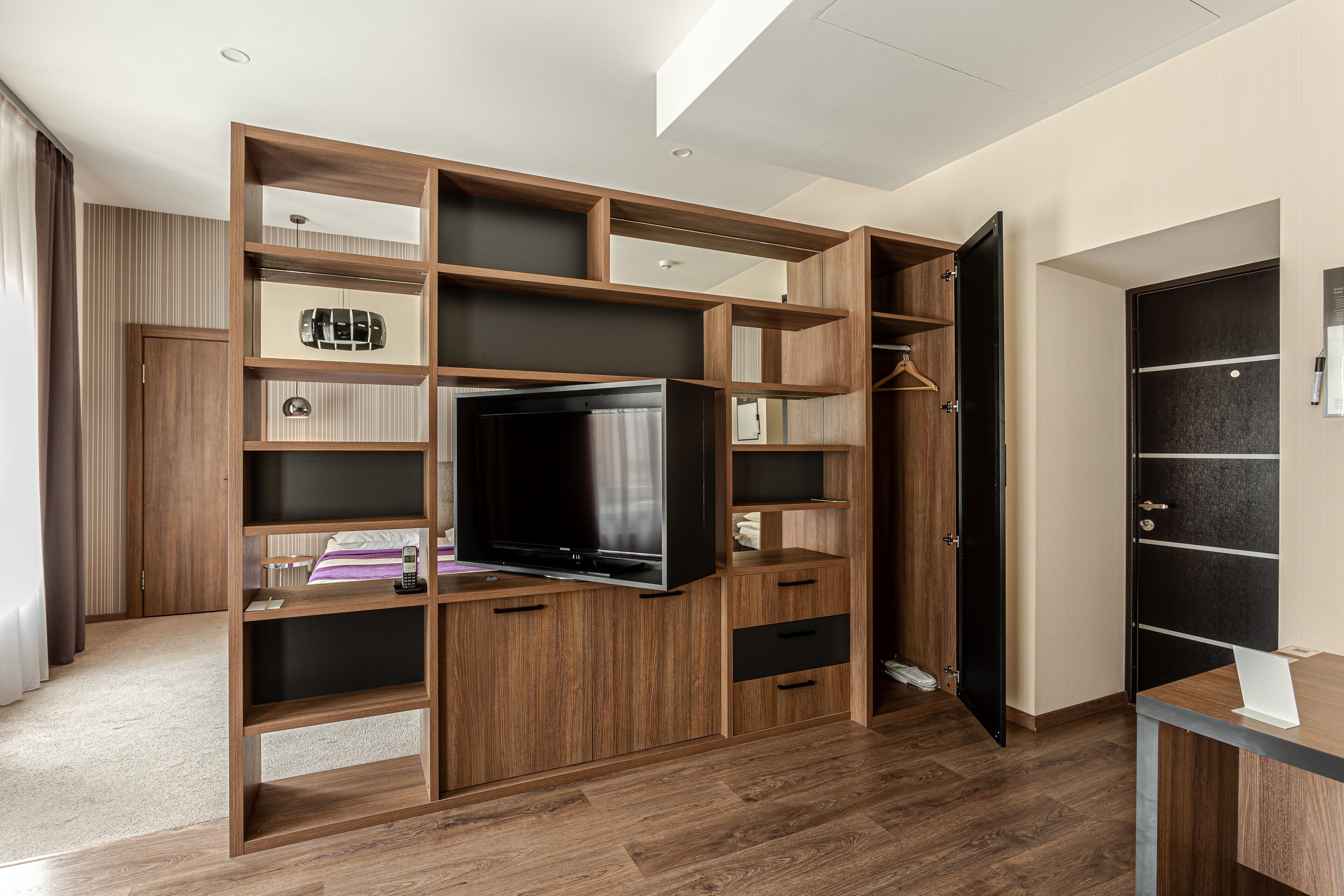 Quarto moderno com TV integrada, estantes de madeira e guarda-roupa.